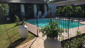 Piscina cercada por grade, com uma casa ao fundo.