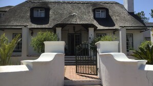 Uma casa com telhado de palha, paredes brancas e um portão que dá acesso à entrada.