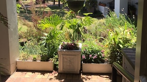 Um alpendre coberto com vista para o jardim, um vaso de flores pendurado e plantas em vasos.