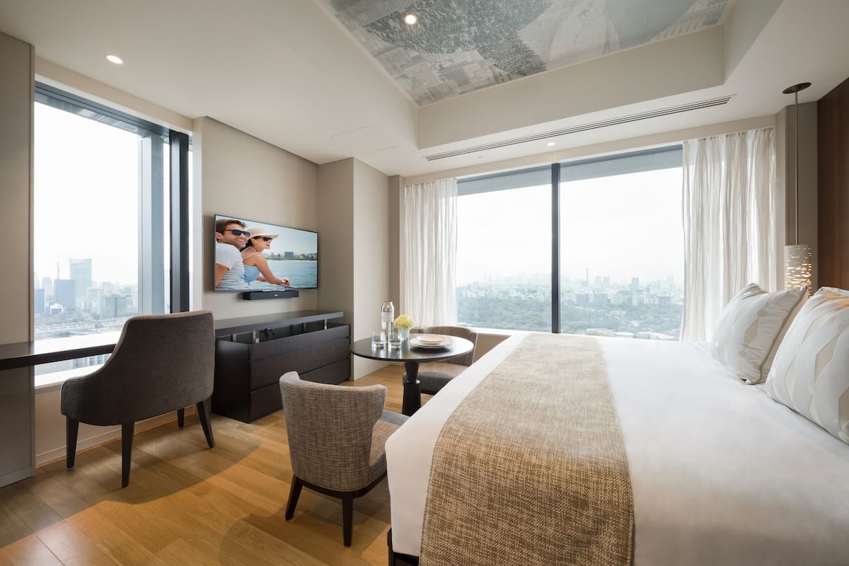 Quarto de hotel com cama grande, escrivaninha com cadeira, televisão e vista para a cidade.