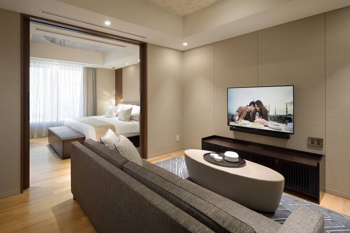 Quarto de hotel moderno com sofá, televisão de tela plana, cama e uma janela grande.