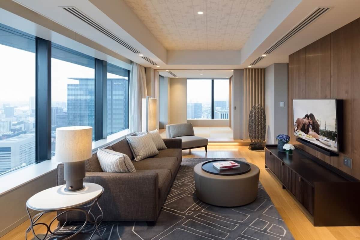 Uma sala de estar moderna com sofá, poltrona, mesa de centro redonda e televisão em parede de madeira.