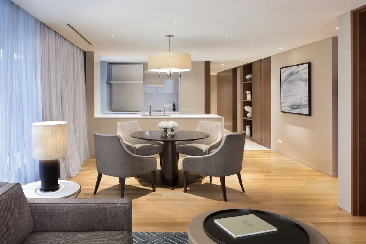 Quarto de hotel moderno com área de refeições, sofá, luminária e vista para a cozinha.