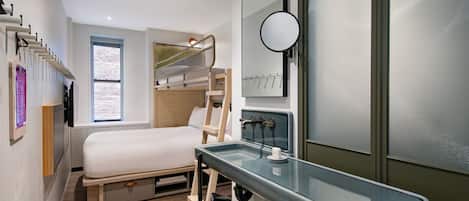 Quarto compacto com beliche, escrivaninha com espelho e janela com persianas.