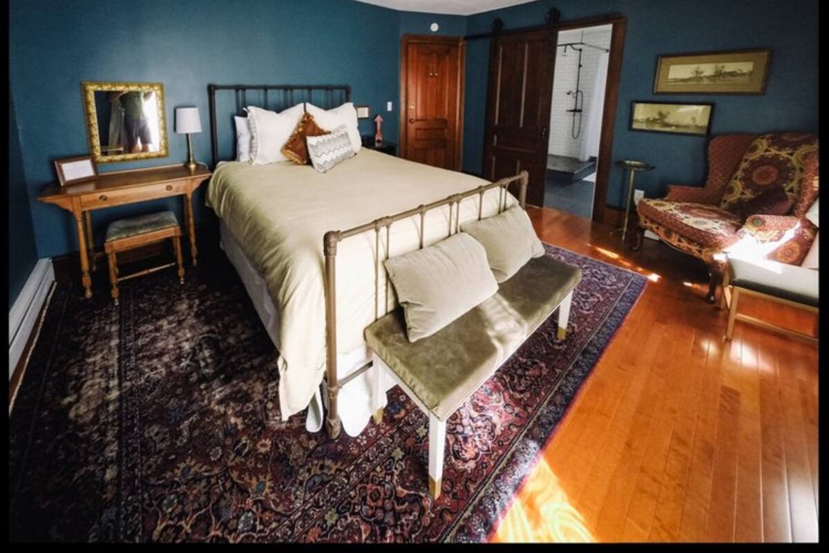 Quarto com uma cama grande, uma mesa de cabeceira de madeira, um banco, uma cadeira e um tapete.