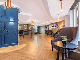 Um hall de hotel moderno com piso de madeira, paredes em azul e mobiliário contemporâneo.