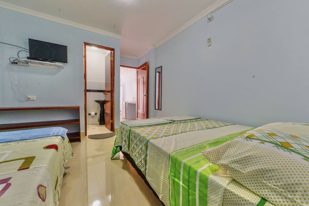 Quarto de hotel com duas camas, uma televisão presa na parede e um banheiro visível por uma porta aberta.