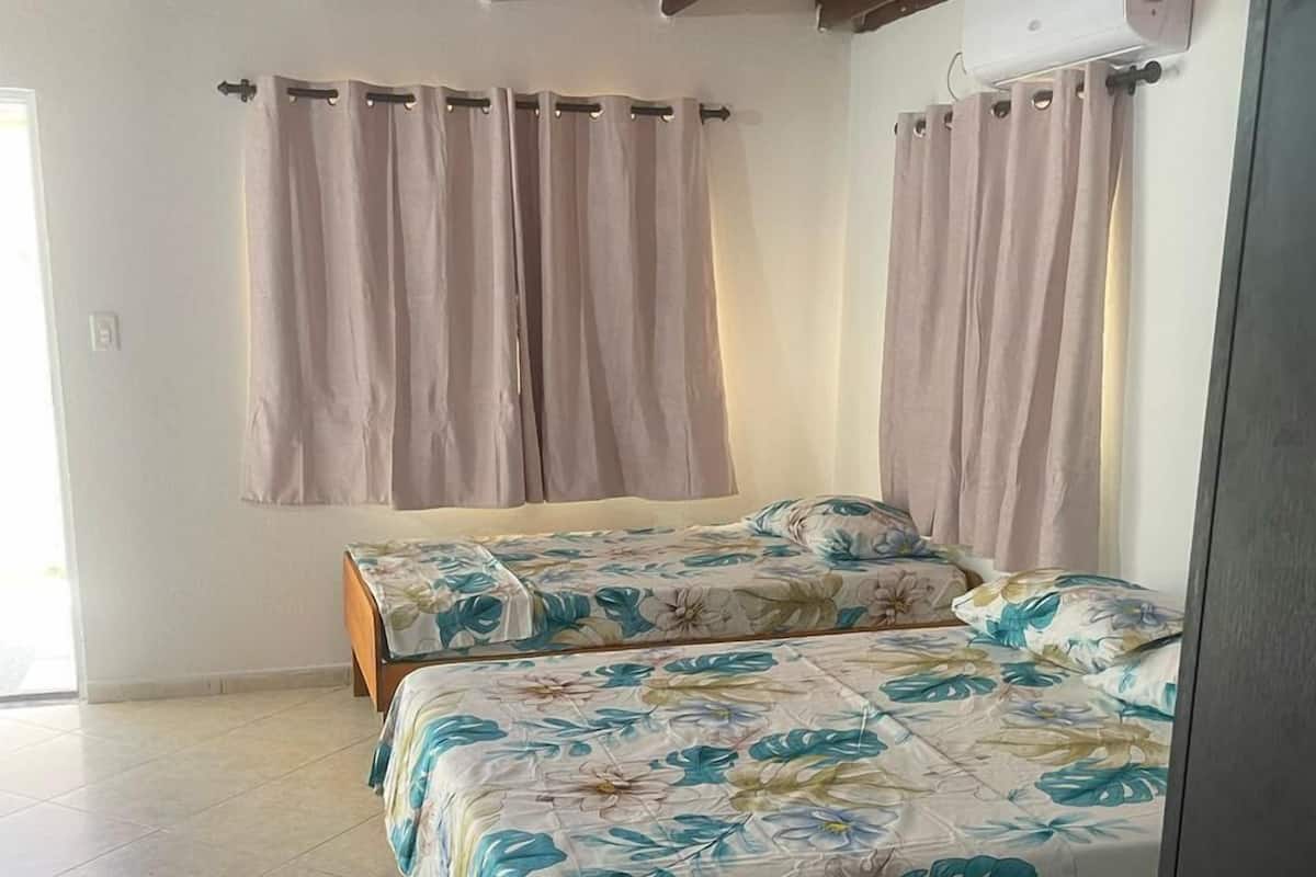 Quarto com duas camas, teto de madeira e cortinas claras.