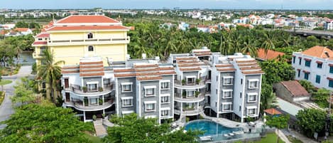 Hotel com vários andares, piscina, rodeado por vegetação e outros edifícios.