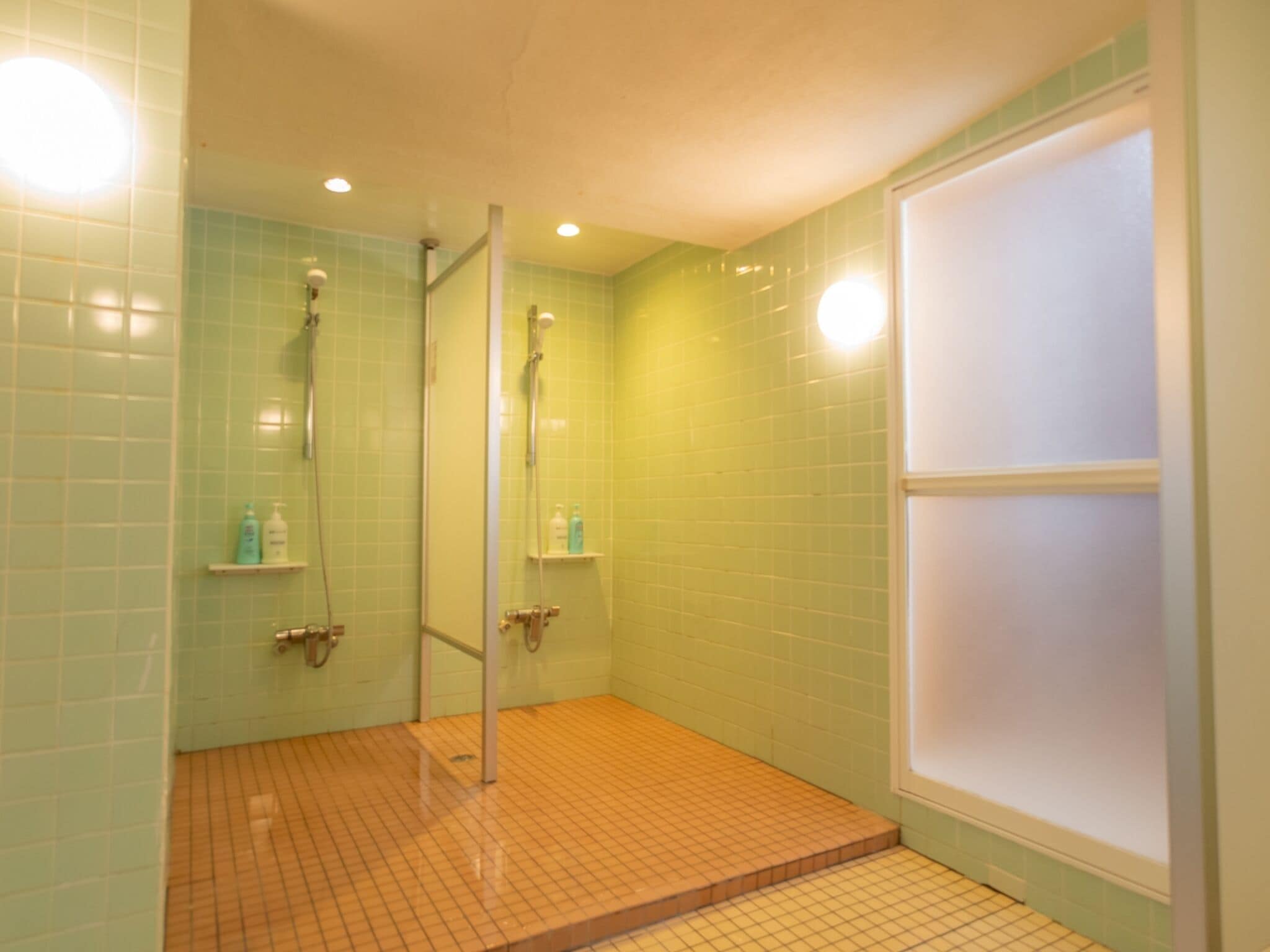 Casa de banho com azulejos verdes, zona de duche e janela.