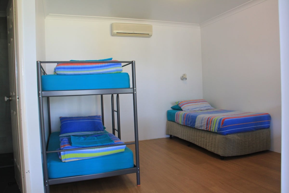 Quarto com uma cama de solteiro e uma beliche, ambas com roupa de cama colorida.