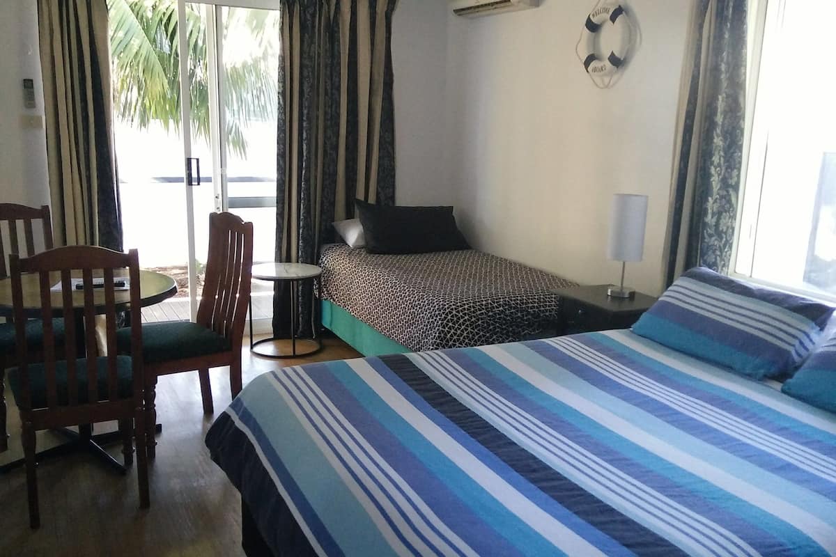 Quarto de hotel com cama, uma cadeira, uma mesinha, janela com cortinas e ar condicionado.