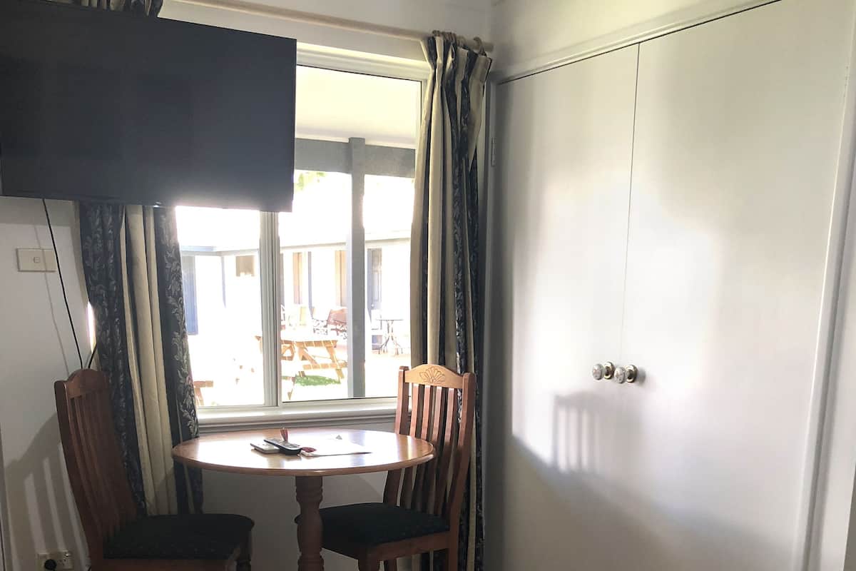 Um quarto com uma cama, uma mesa, duas cadeiras, uma televisão e um guarda-roupa.