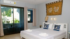 Quarto de hotel com uma cama grande, porta de vidro deslizante para a varanda e uma tapeçaria decorativa de elefante na parede.