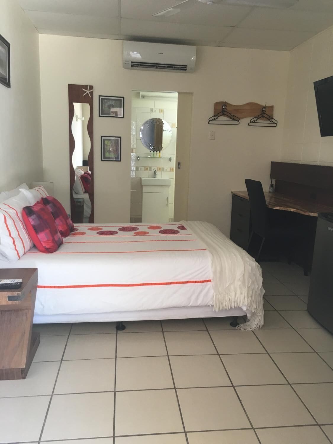 Quarto de hotel com cama, escrivaninha, cadeira, espelho e ar condicionado.