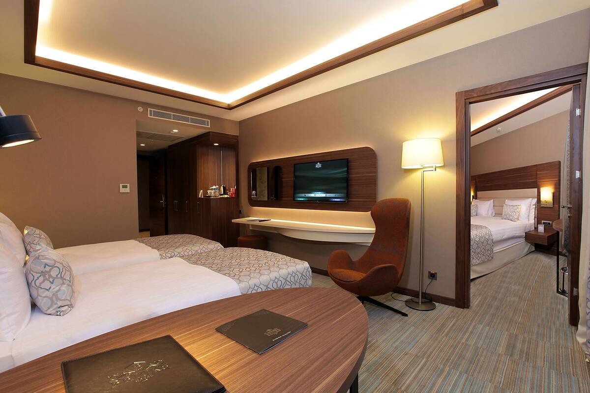 Quarto de hotel com duas camas, uma escrivaninha, uma televisão, uma cadeira e um espelho.
