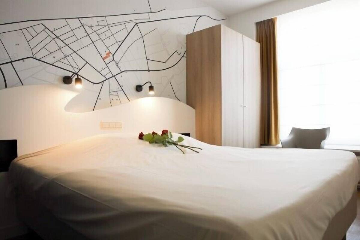Cama bem arrumada com um mapa na parede, abajur e um buquê de flores.