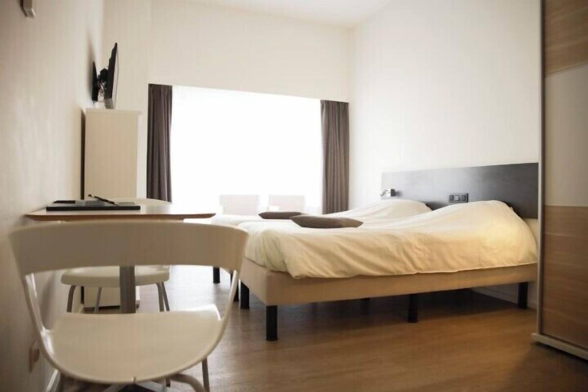 Quarto de hotel com uma cama, uma escrivaninha e uma cadeira.