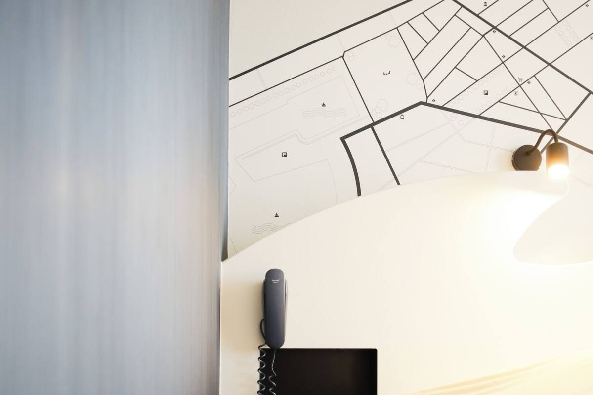 Quarto de hotel com uma cama, telefone fixado na parede e um mapa na parede.