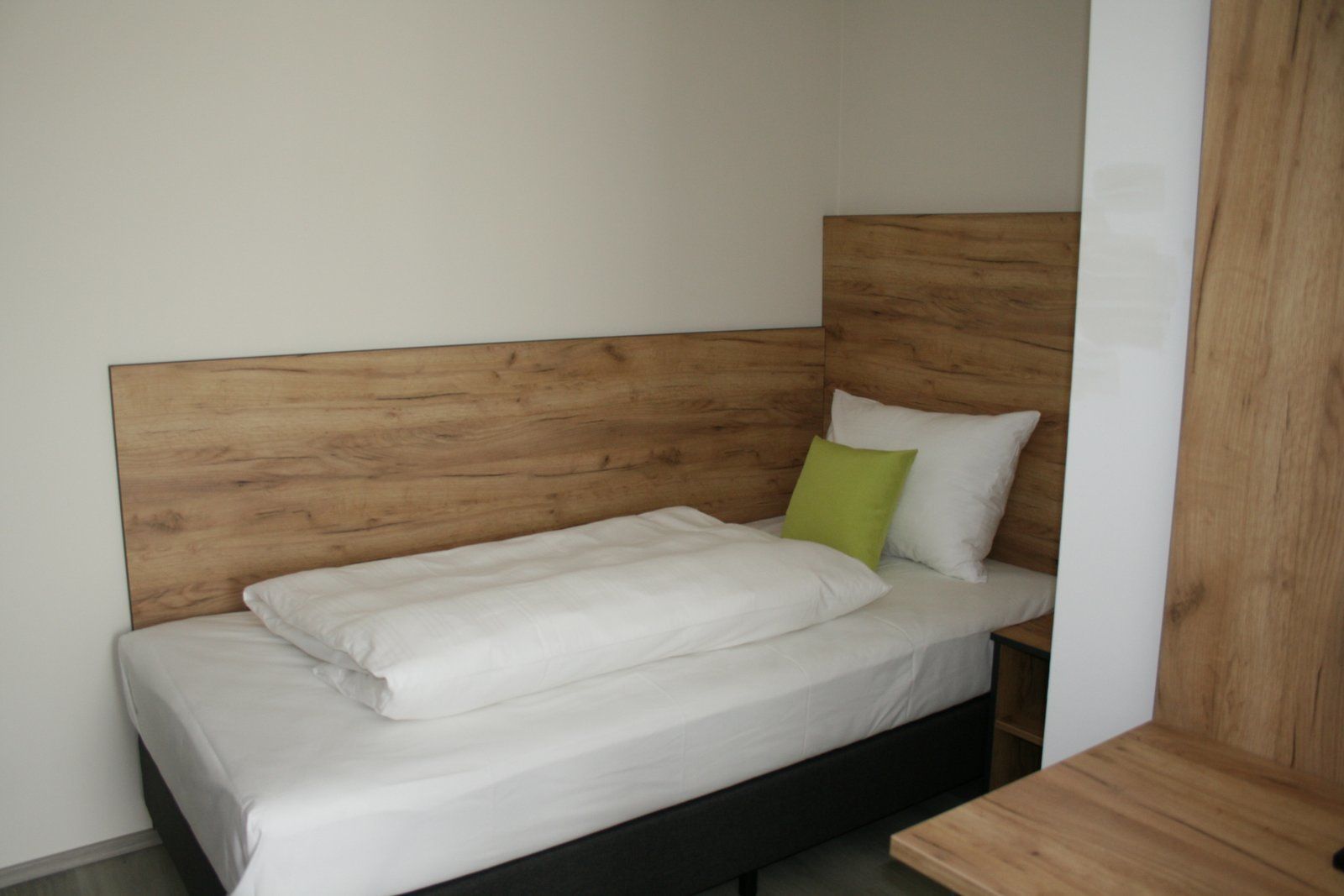 Uma cama de solteiro com cabeceira de madeira, roupa de cama branca e travesseiro verde.