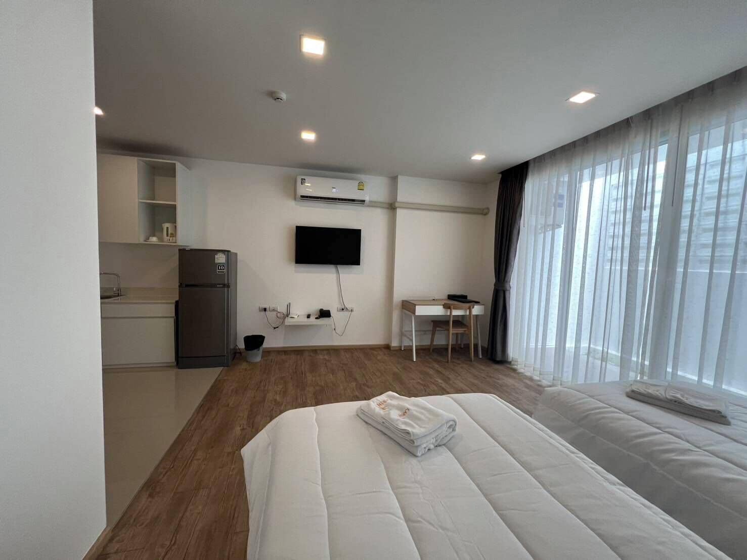 Quarto de hotel com cama, escrivaninha, televisão e cozinha compacta.