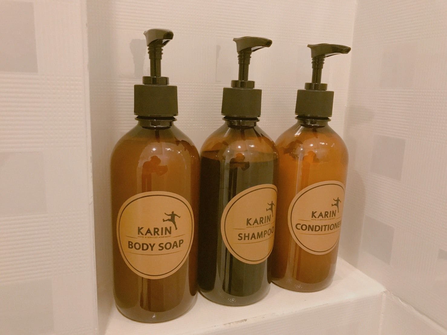 Três frascos de sabonete líquido, shampoo e condicionador Karin em uma prateleira.