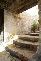 Uma escadaria de pedra que leva a um nível superior, com um candeeiro suspenso e uma pequena árvore ao fundo.