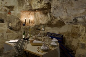 Quarto com paredes de pedra, mesa posta para refeição, velas e uma garrafa de vinho.