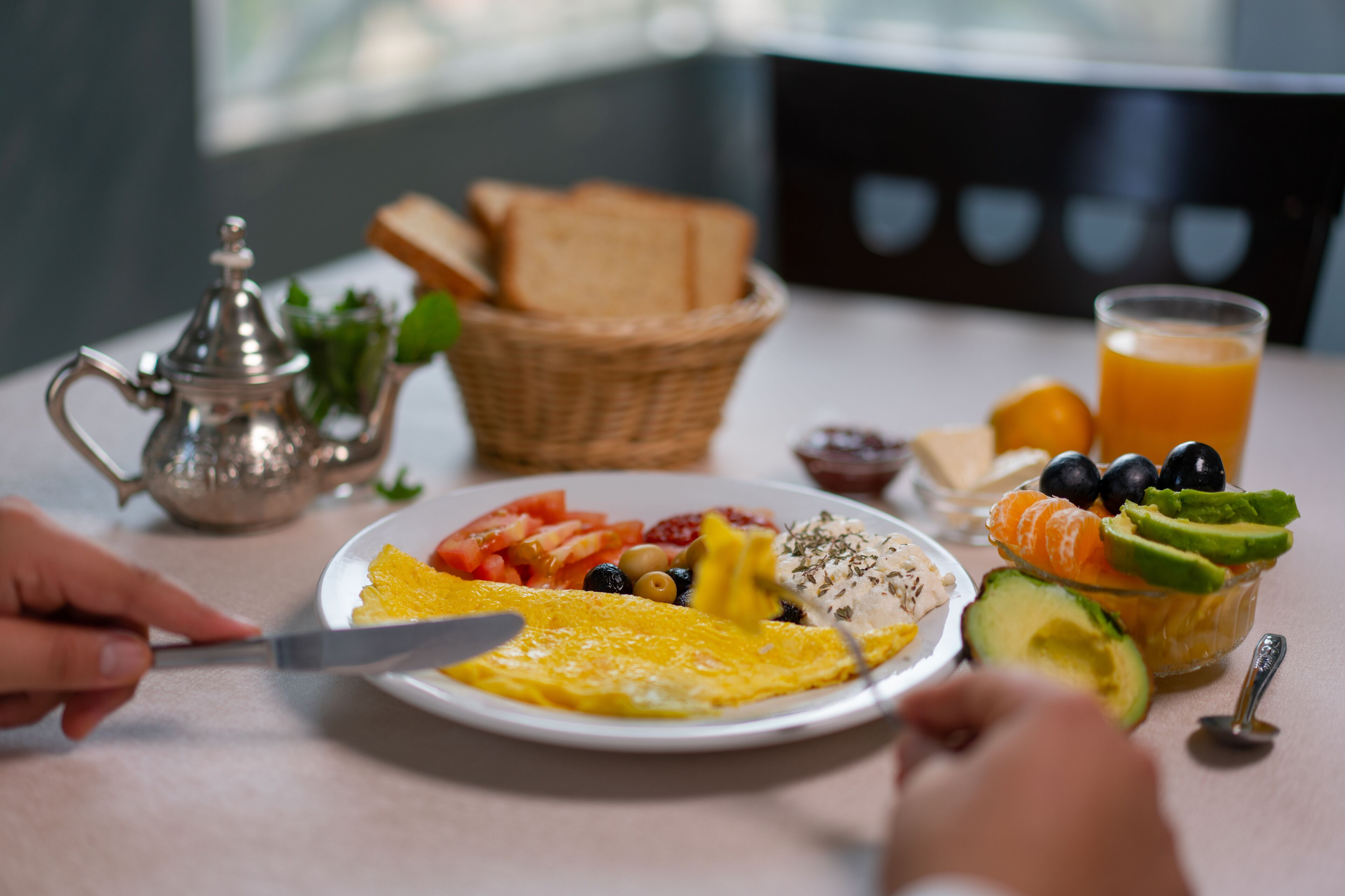 Mesa de café da manhã com prato de comida, um bule e um copo de suco de laranja.