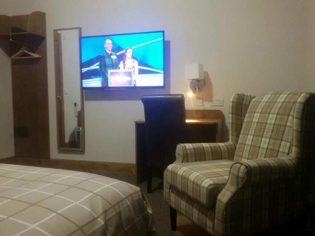 Quarto de hotel com cama, poltrona xadrez, televisão e uma pequena mesa.