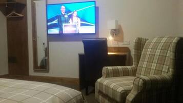 Quarto de hotel com cama, poltrona xadrez, televisão e uma pequena mesa.