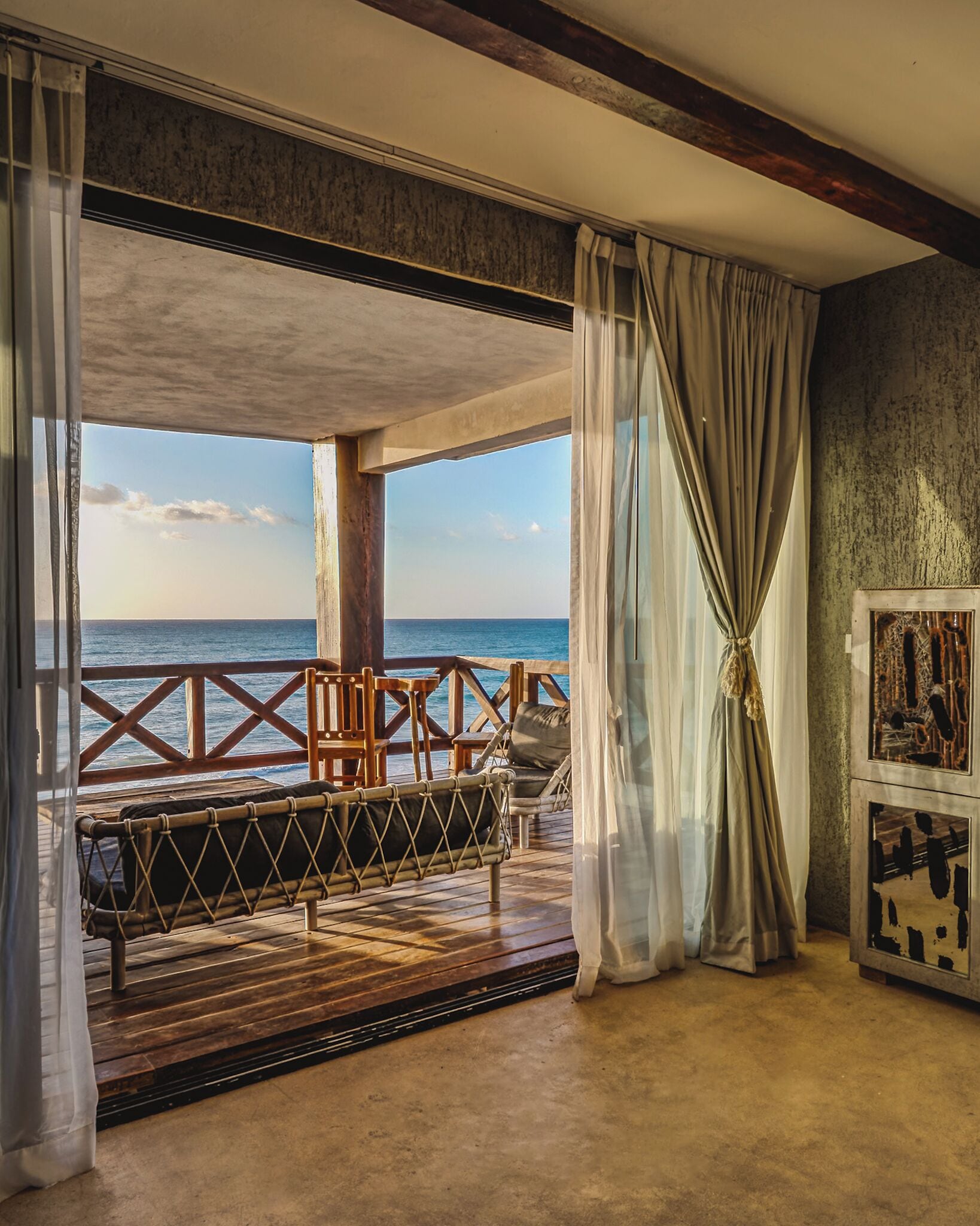 Quarto com vista para o mar, um deck de madeira e uma janela grande com cortinas.