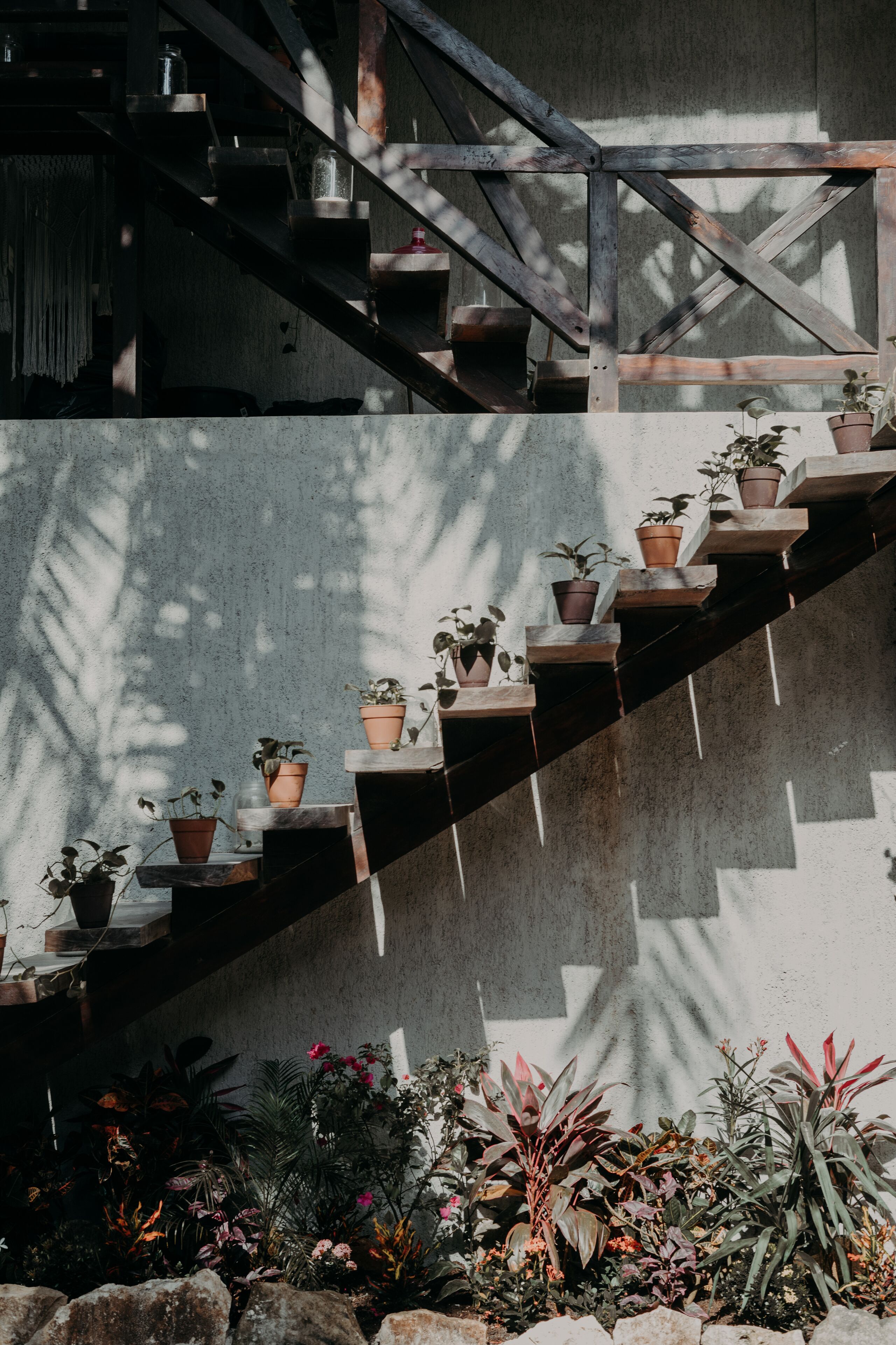 Uma escadaria com vasos de plantas em cada degrau, conduzindo a um nível inferior com mais plantas e pedras.