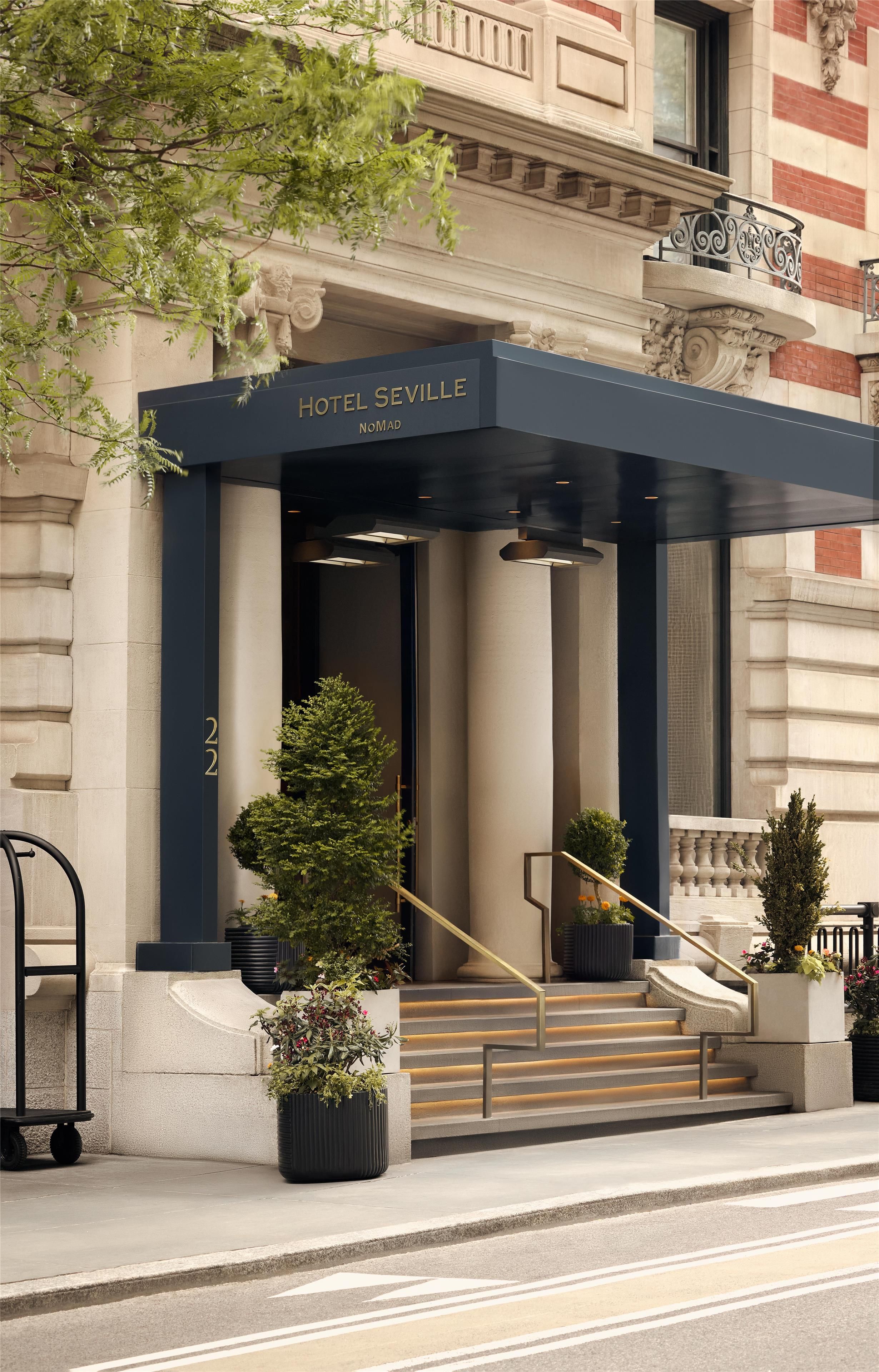 Entrada de hotel com toldo azul escuro, escadaria e placa com a inscrição 'HOTEL SEVILLE'.