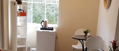 Um espaço de estar compacto com sofá, mesa de jantar com cadeiras, cozinha com geladeira e janela que proporciona iluminação natural.