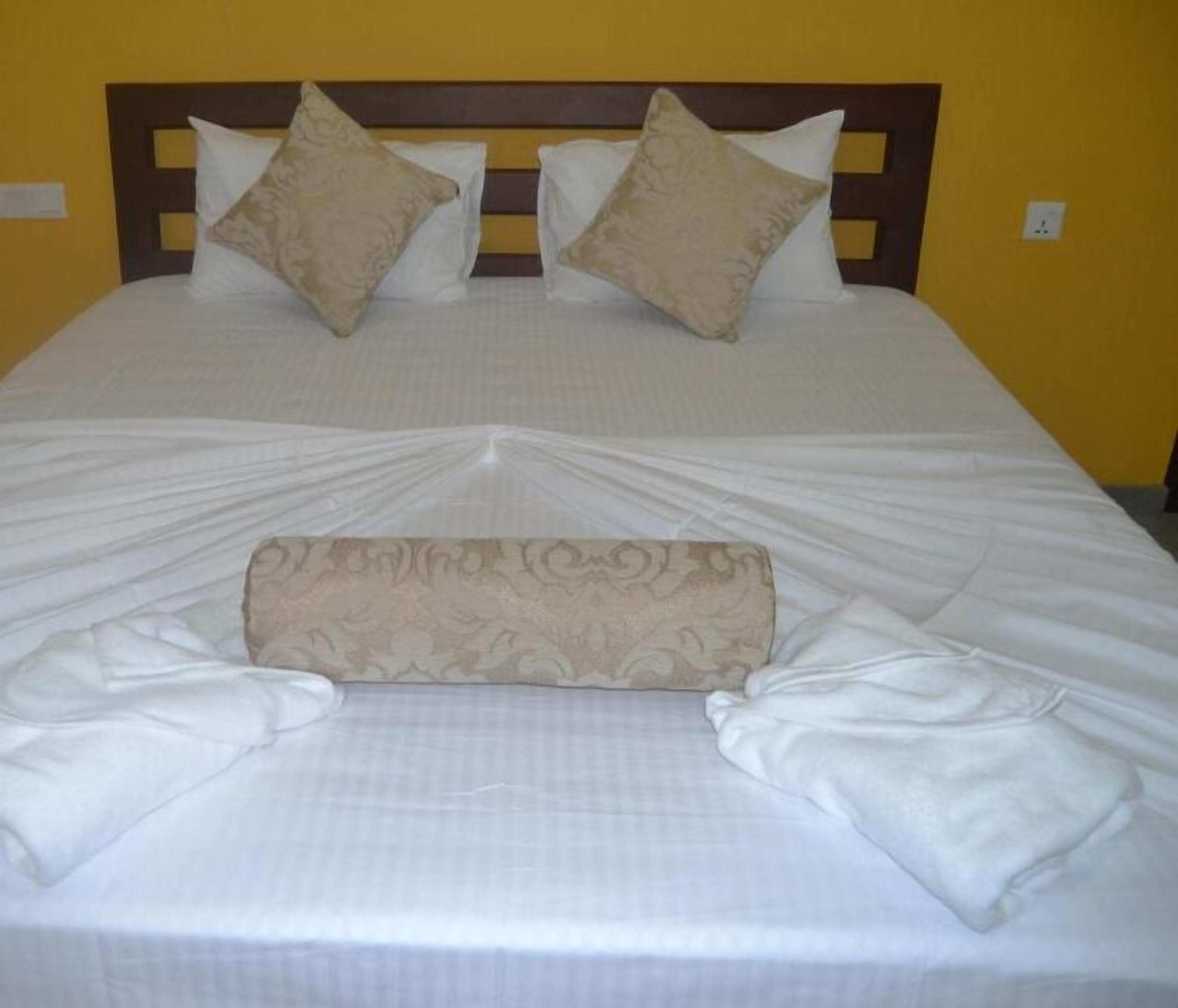 Cama bem arrumada com travesseiro estampado e dois travesseiros lisos, em frente a uma parede amarela.