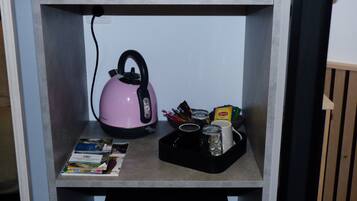 Uma cozinha compacta com uma chaleira rosa, uma cafeteira, uma caneca e uma bandeja com um saquinho de chá Lipton e um livro.
