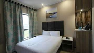 Quarto de hotel com cama, mesa de cabeceira, pequena mesa, guarda-roupa e um quadro na parede.