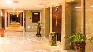 Um saguão de hotel com piso de mármore, dois elevadores e plantas em vasos.