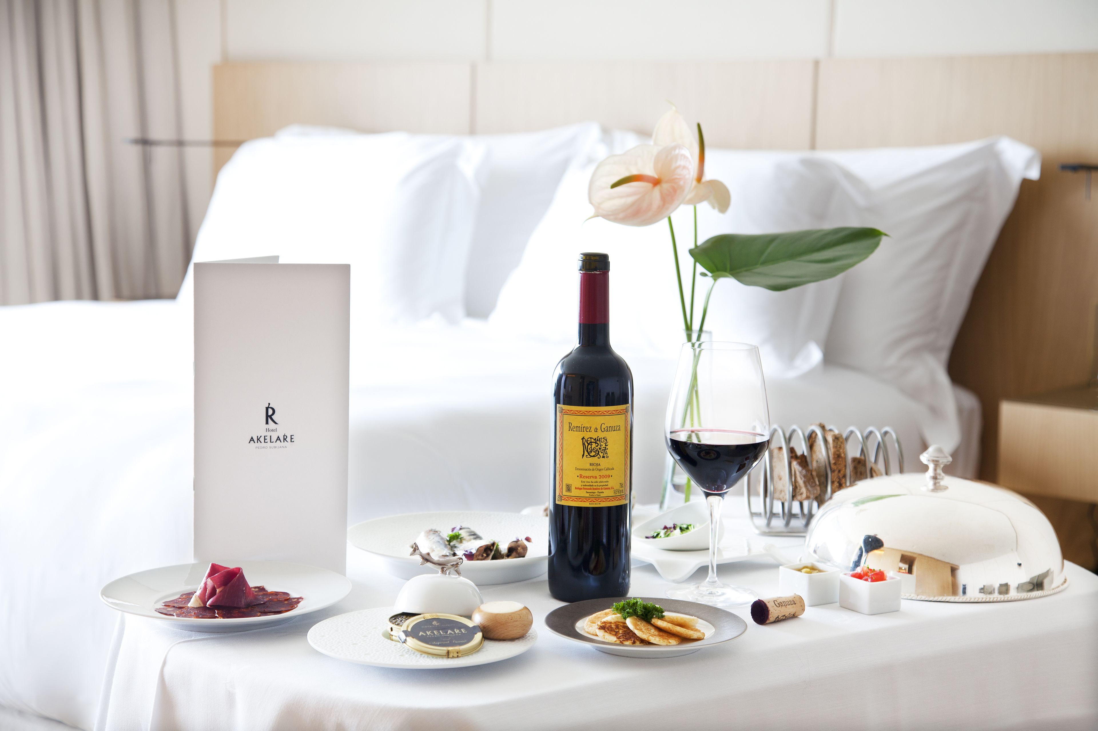 Uma mesa bem arrumada com uma garrafa de vinho, um copo de vinho tinto, uma flor branca e diversos pequenos pratos com comida.