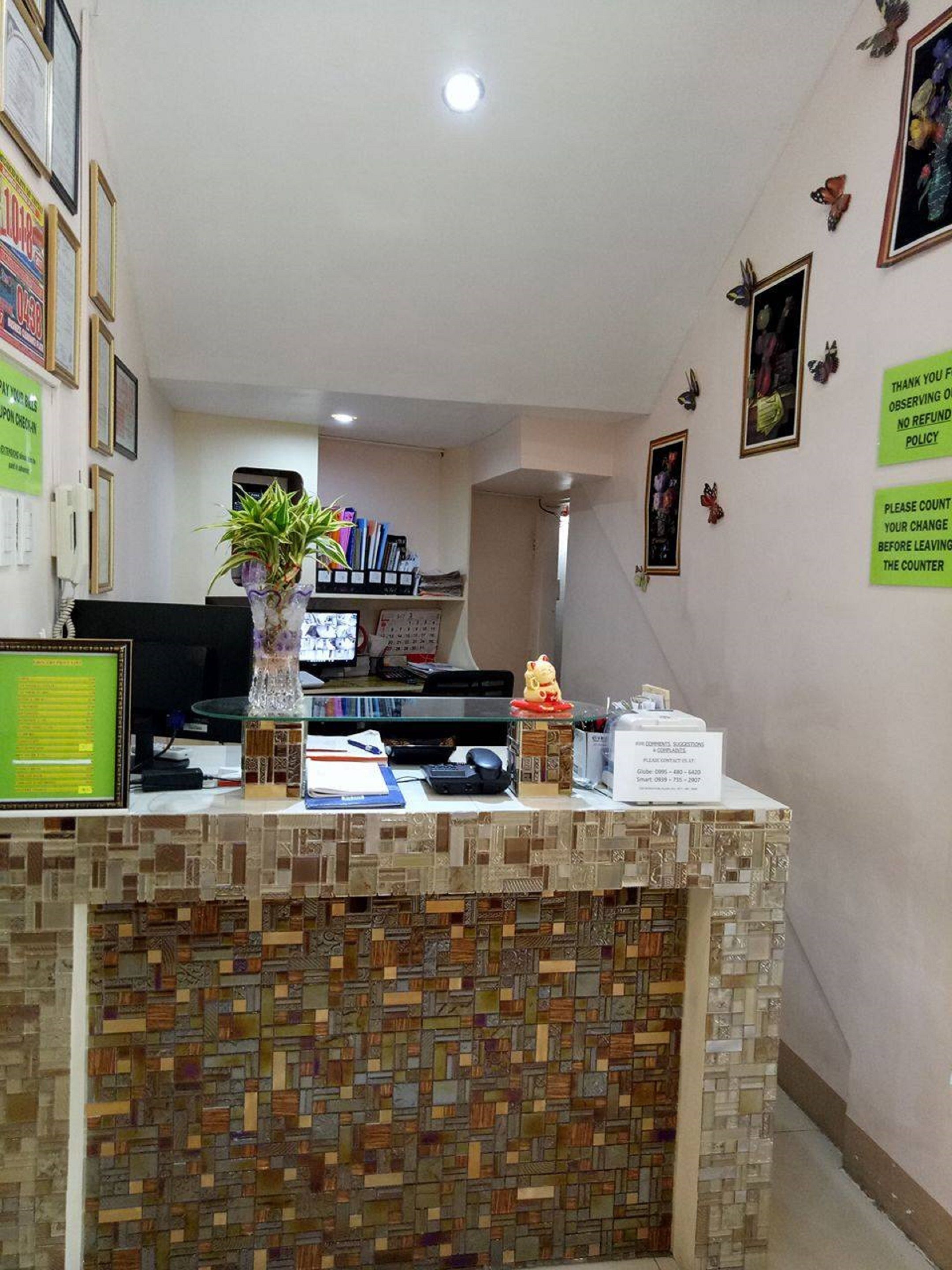 Bancada de recepção com design em mosaico, um computador, uma planta e diversos avisos nas paredes.