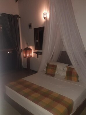 Quarto com cama, mesa de cabeceira, luminária e janela com cortinas.