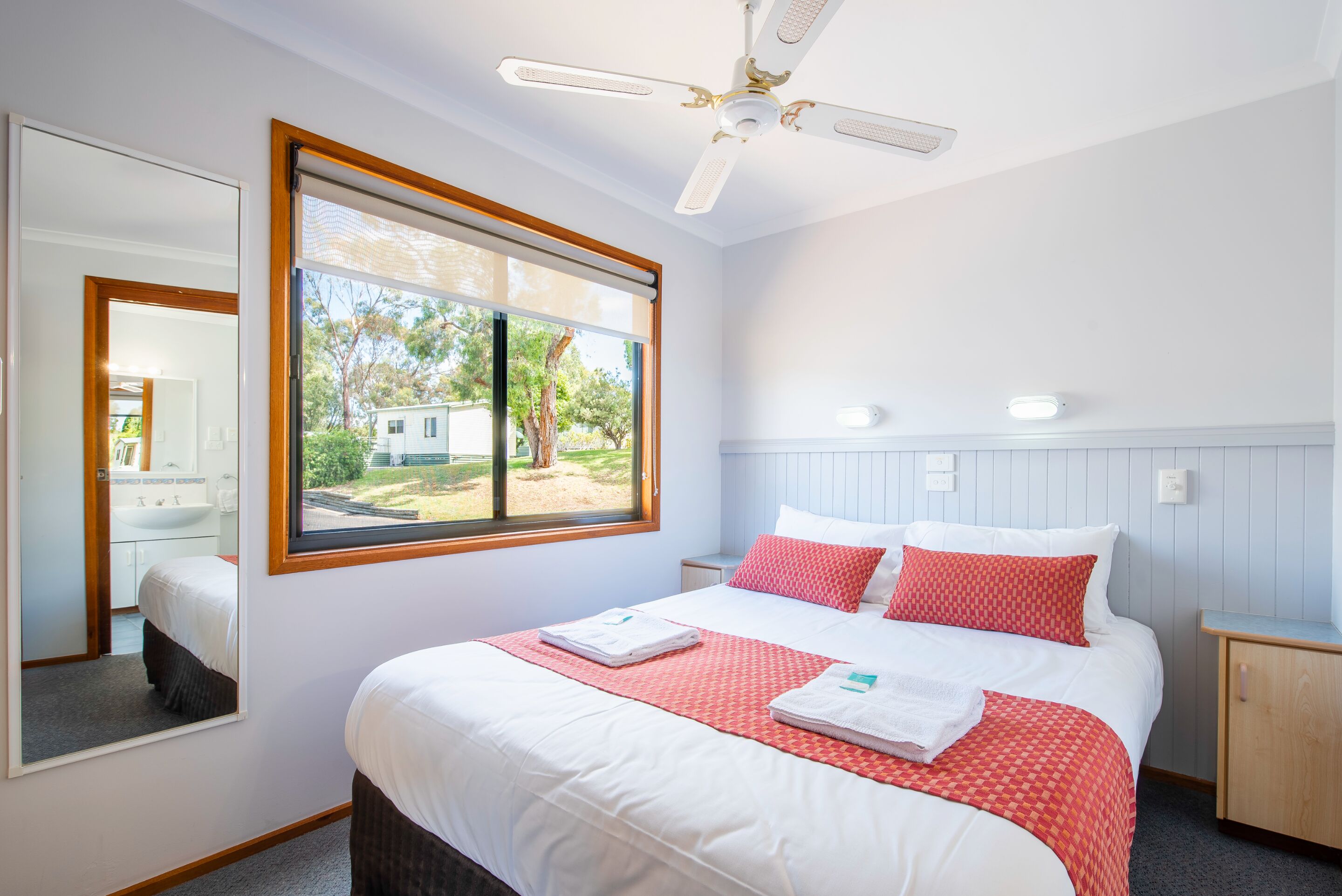 Quarto com cama grande, janela com vista para o exterior, ventilador de teto e mesa de cabeceira.