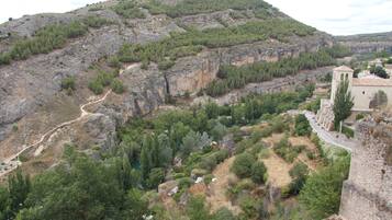 Paisagem montanhosa com um caminho serpenteante, um edifício de pedra com um campanário e vegetação densa.