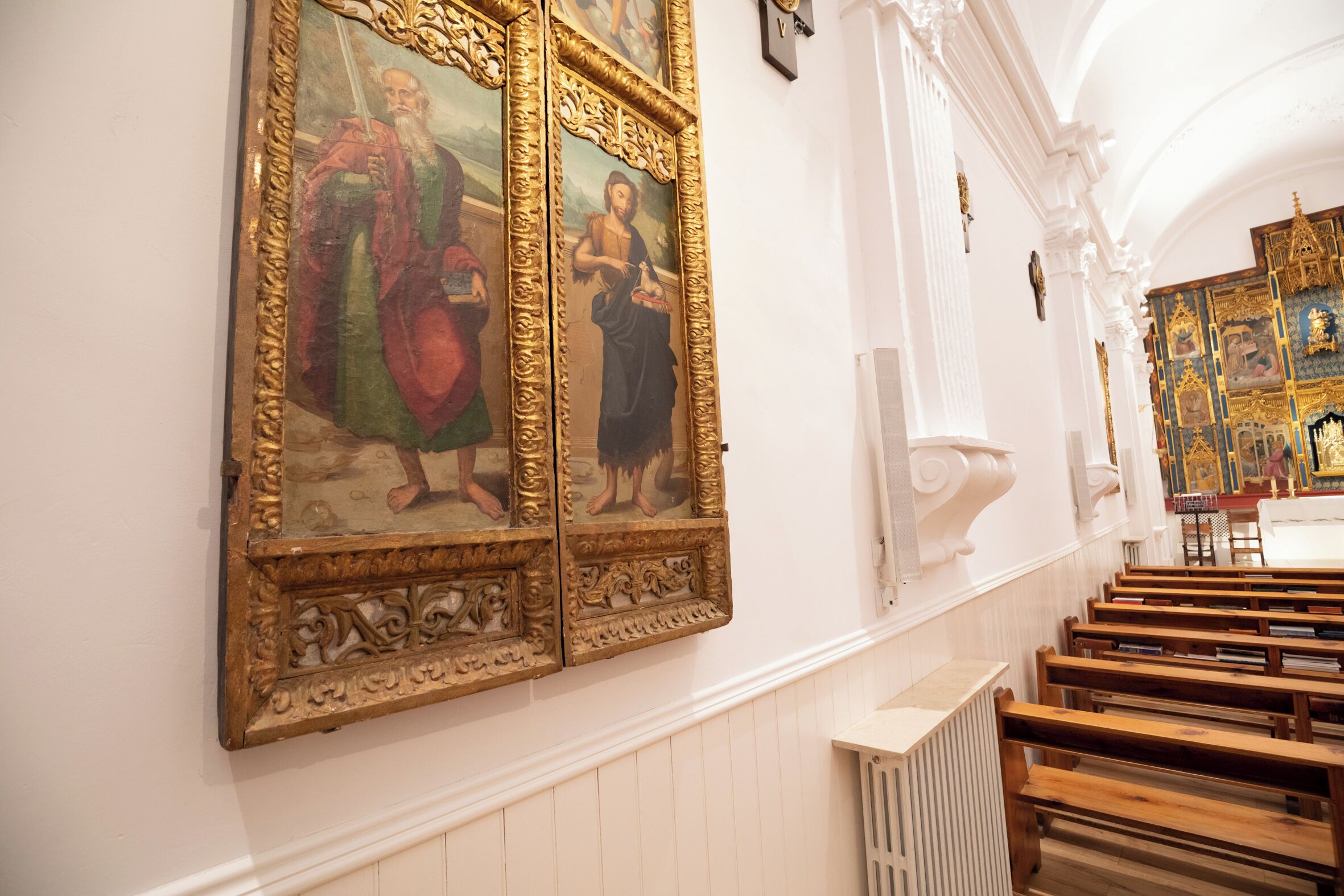 Interior de igreja com bancos de madeira e uma grande pintura religiosa na parede.