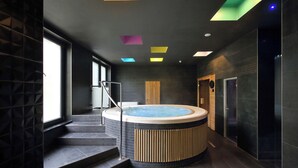 Uma área de spa moderna com hidromassagem, paredes revestidas de azulejos e uma escadaria que leva a uma porta de madeira.