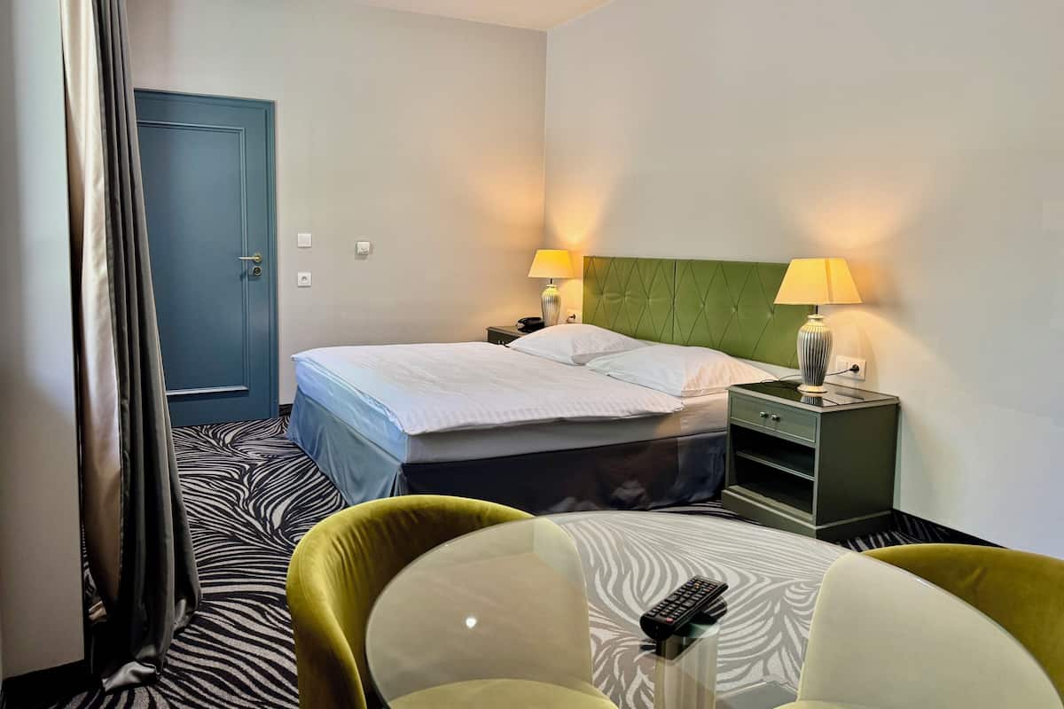 Quarto de hotel com cama, duas luminárias de cabeceira, mesa de cabeceira, mesa e duas cadeiras.