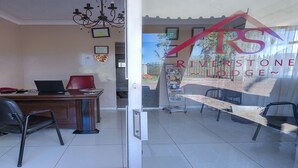 Um escritório moderno com uma mesa, cadeiras e uma televisão. Uma porta de vidro dá acesso a uma área externa com uma placa para Riverstone Lodge.