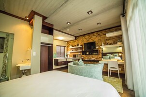 Quarto de hotel com cama, escrivaninha, televisão e parede de tijolos.