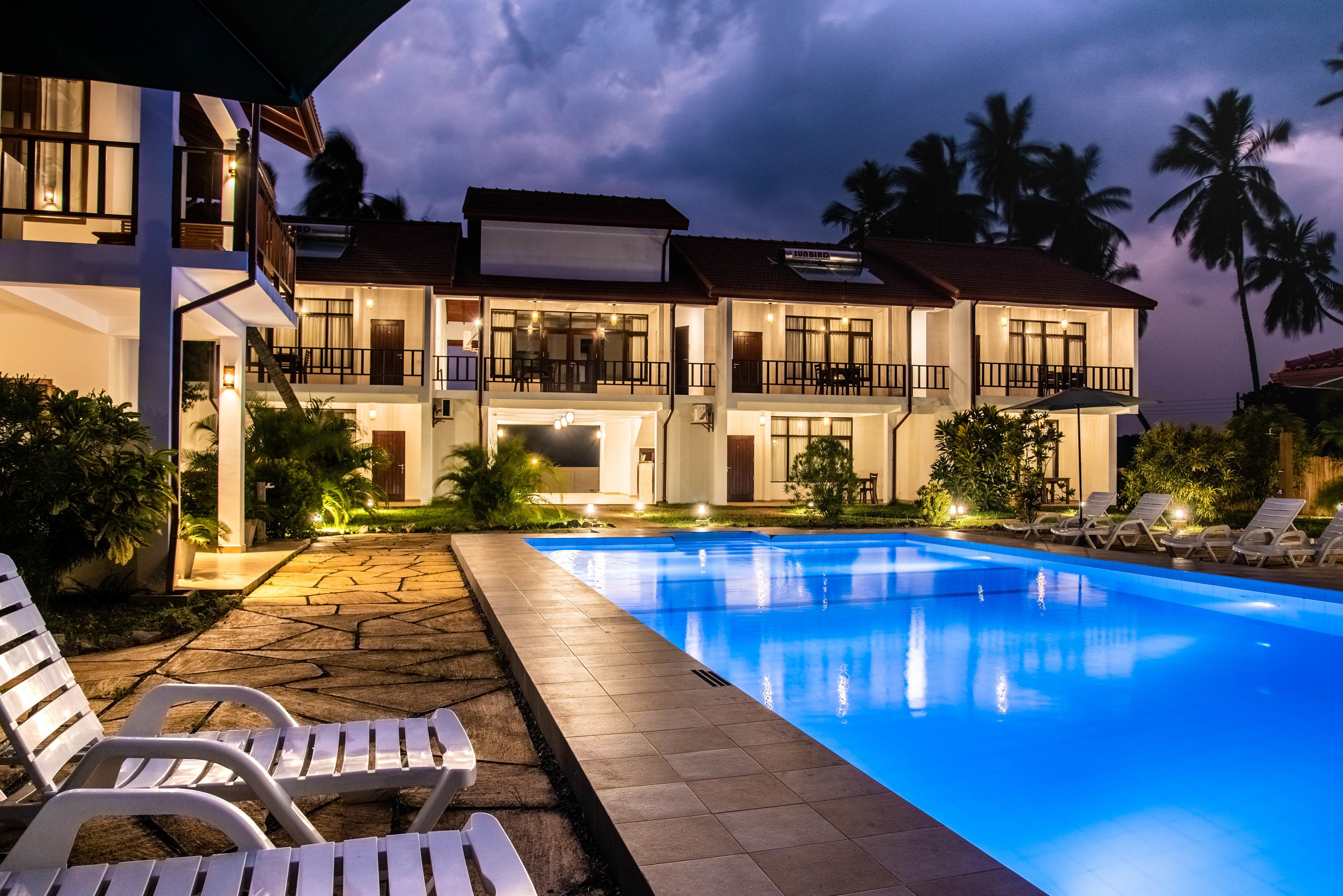Um hotel com vários andares, piscina, área de estar externa e palmeiras.